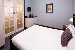 Quarto de hotel com cama, escrivaninha com computador, televisão na parede e quadro decorativo.