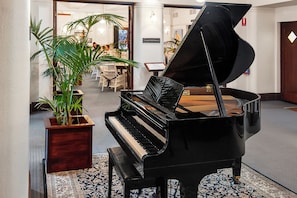 Um piano de cauda em uma área de recepção, com um vaso de planta ao lado.