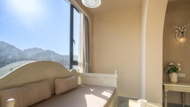Um quarto com uma cama encostada na parede, uma janela com vista para montanhas, uma luminária em formato de cabeça de veado fixada na parede, e uma pequena mesa com um vaso.