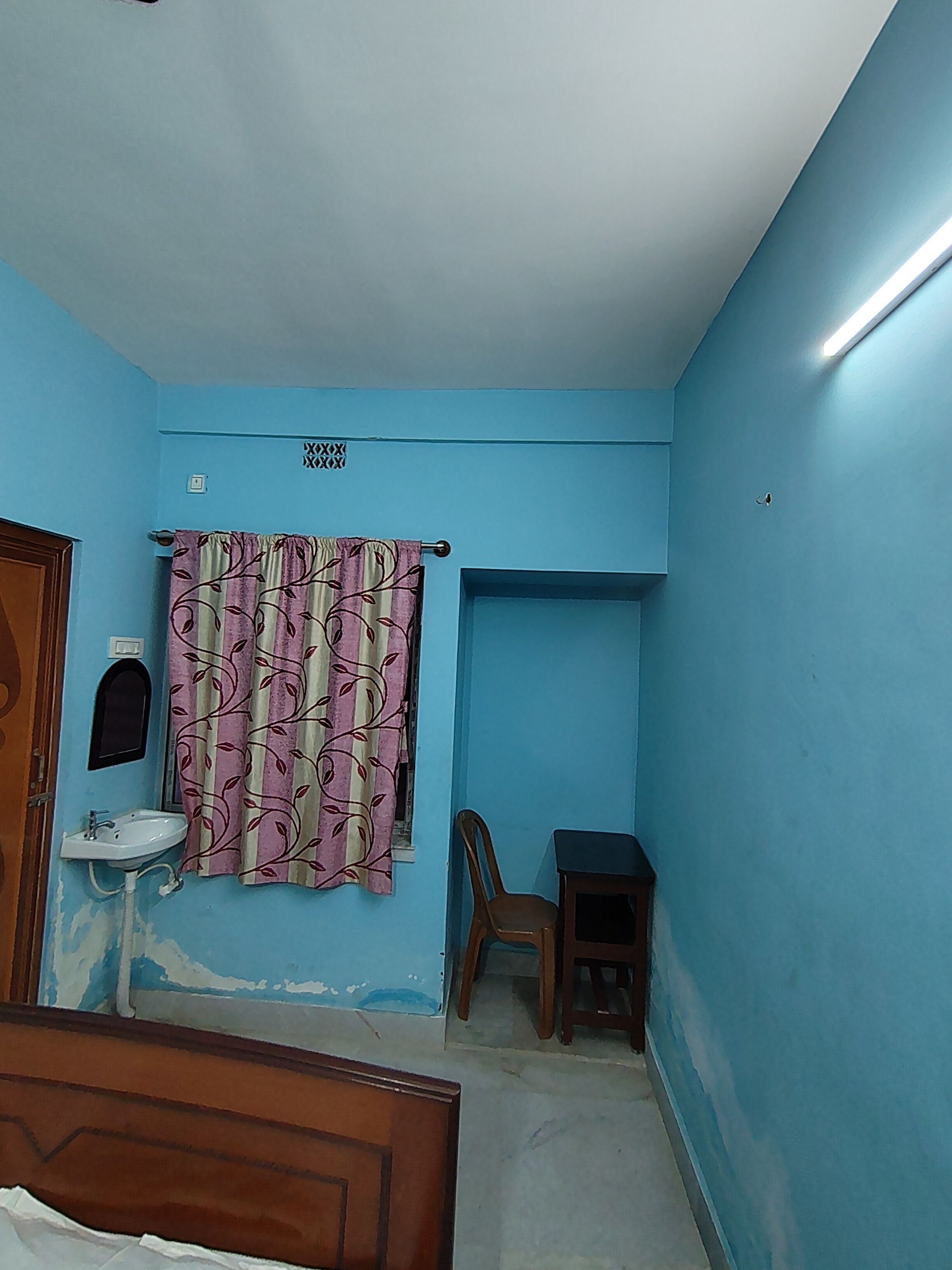 Um quarto com cama, pia, cadeira e janela com cortinas.