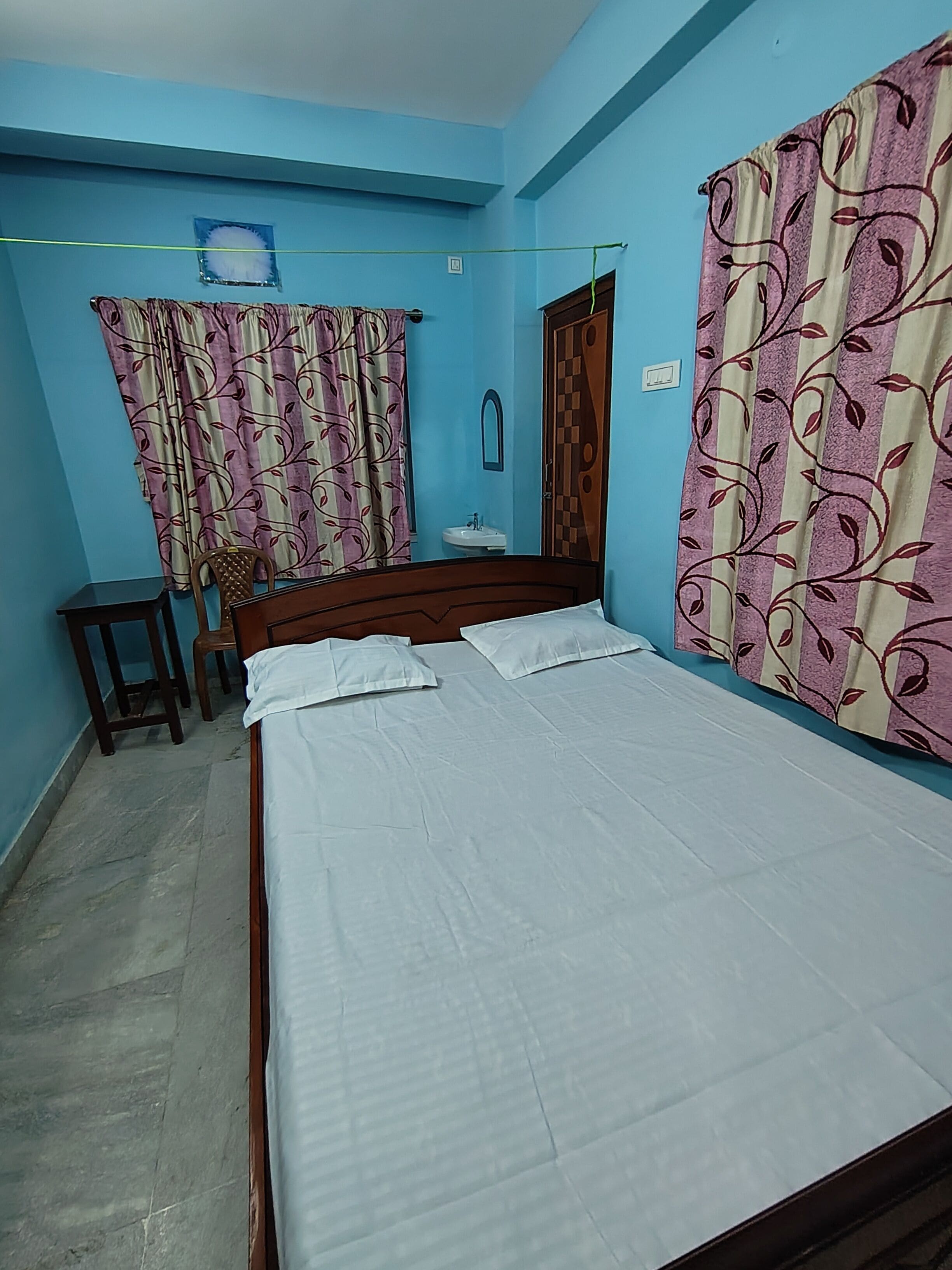 Quarto com uma cama, cabeceira de madeira, mesa de cabeceira, uma cadeira, uma mesinha e um espelho.