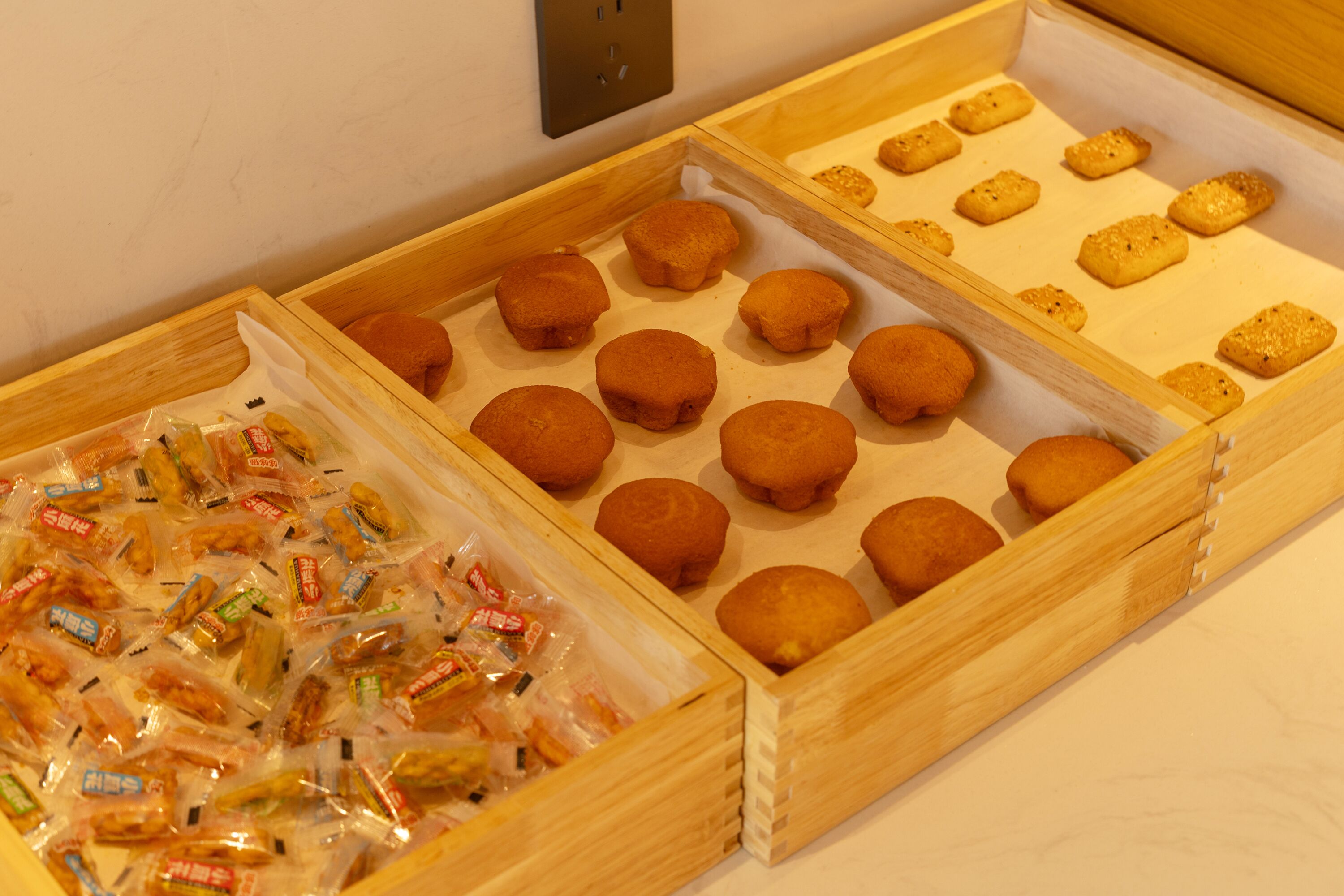 Vitrine de madeira com diversos petiscos e produtos de panificação embalados.
