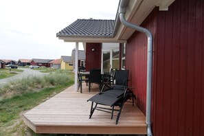 Um deck de madeira com mobiliário externo, uma área de varanda coberta e vista para casas vizinhas.