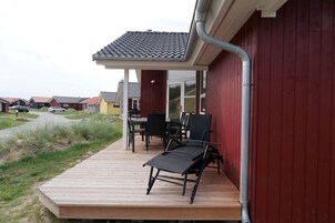 Um deck de madeira com mobiliário externo, uma área de varanda coberta e vista para casas vizinhas.