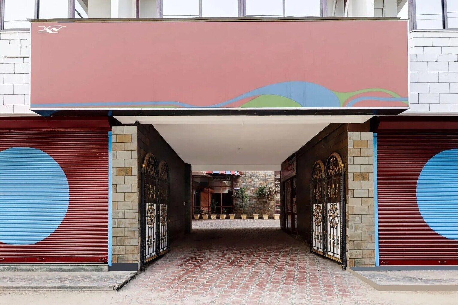 Entrada de um edifício com varanda coberta, portões de metal decorativos e chão de azulejos.