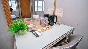 Quarto de hotel com escrivaninha, um vaso de planta, um controle remoto, uma bandeja com xícaras de café, uma cafeteira e um estojo de lenços.