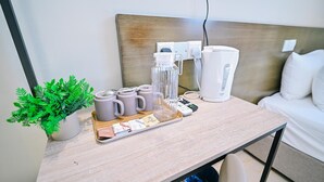 Quarto de hotel com cabeceira de madeira, uma mesinha com uma bandeja de itens de café da manhã, uma planta em vaso e um sofá branco.