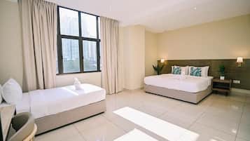 Quarto de hotel com duas camas, um sofá, uma escrivaninha e uma janela grande com cortinas.