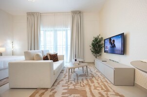 Quarto de hotel moderno com sofá, mesa de centro, TV fixada na parede e uma grande janela com cortinas.