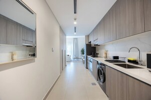 Uma cozinha moderna com máquina de lavar embutida, pia e uma área de refeições visível ao fundo.