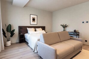 Quarto moderno com cama, mesas de cabeceira, um sofá, uma planta em vaso e um quadro na parede.