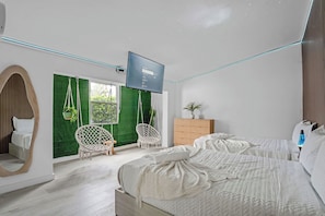 Quarto moderno com cama, duas cadeiras penduradas, uma TV e um armário de madeira.