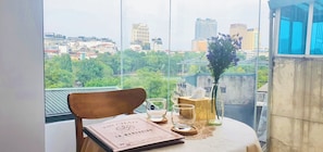 Uma mesa com uma cadeira, um livro e um copo em uma varanda com vista para a cidade.