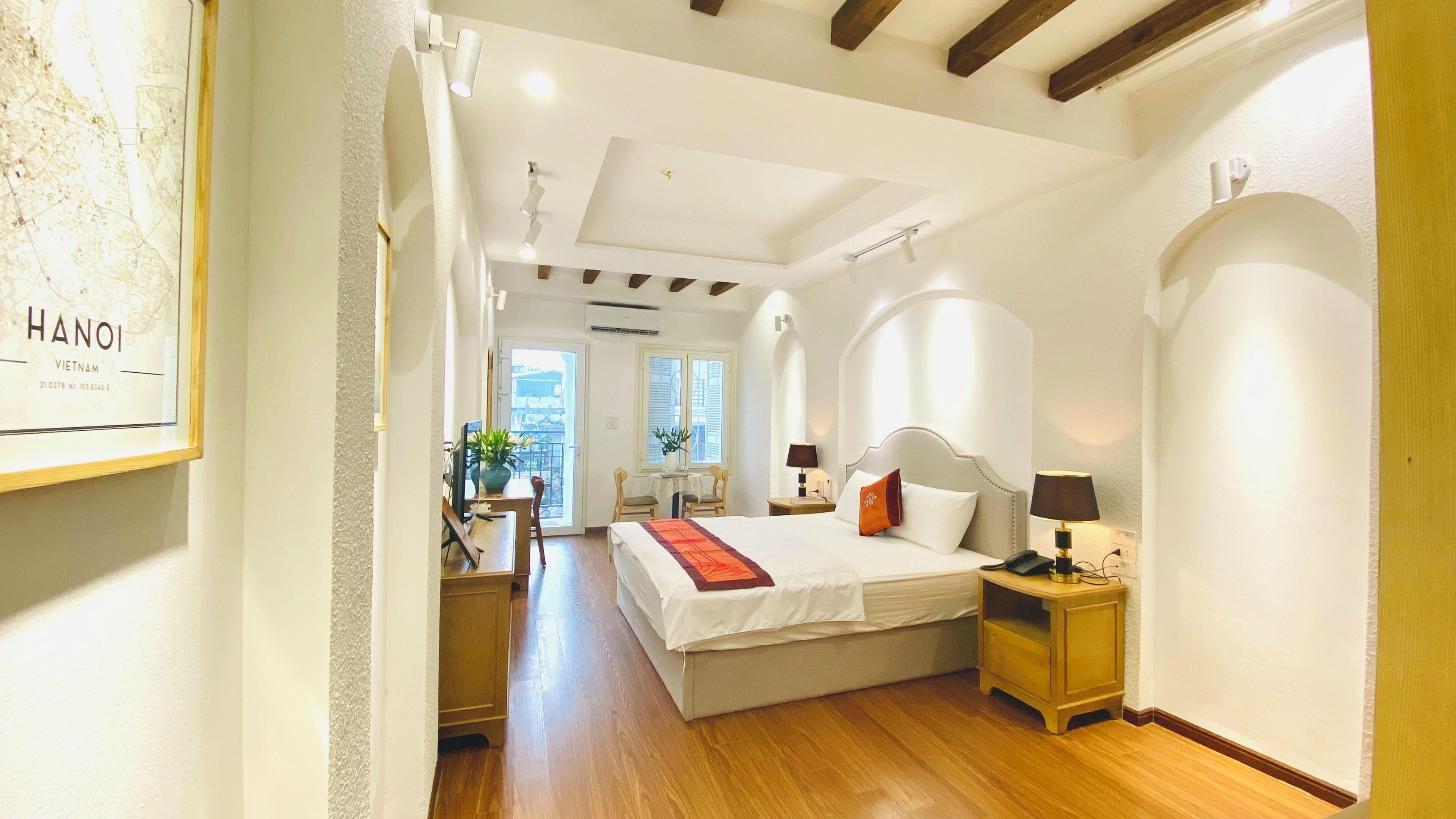 Quarto de hotel com cama, mesas de cabeceira, escrivaninha com cadeira, janela e um mapa emoldurado na parede.