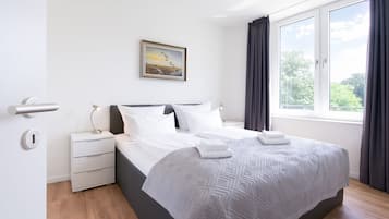 Um quarto moderno com uma cama grande, uma mesinha de cabeceira, uma luminária na parede e uma cortina na janela, além de um quadro pendurado na parede.