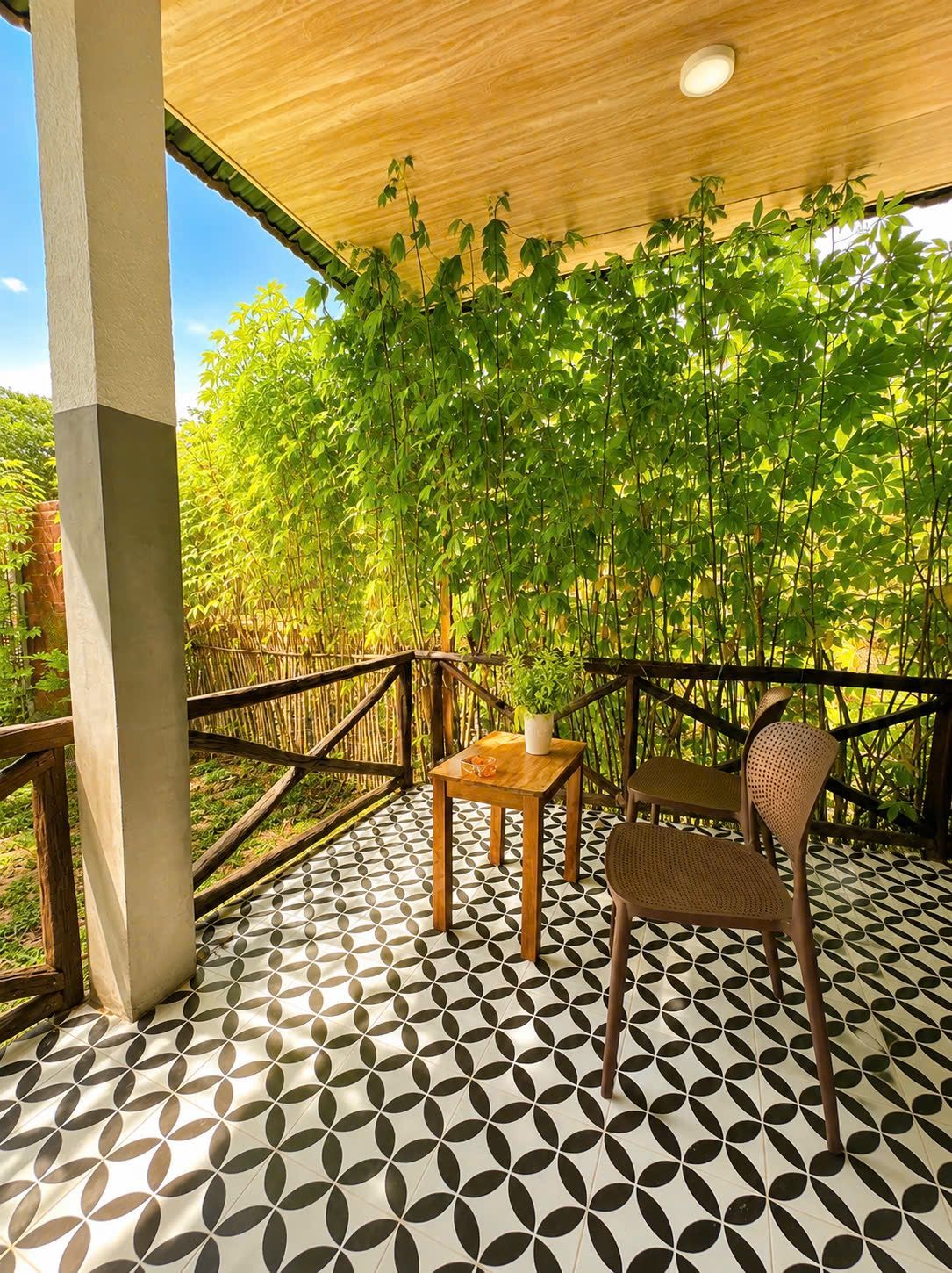 Um pátio externo com piso estampado, mesa de madeira, cadeira de vime e cerca de bambu.