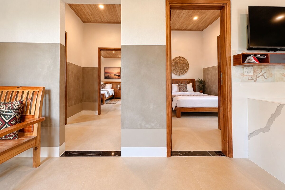 Quarto de hotel com um banco de madeira, uma cama com cabeceira, uma televisão e uma prateleira fixada na parede.