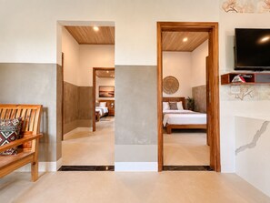 Quarto de hotel com um banco de madeira, uma cama com cabeceira, uma televisão e uma prateleira fixada na parede.