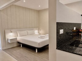 Quarto de hotel moderno com uma cama grande, mesas de cabeceira e banheiro com bancada preta.