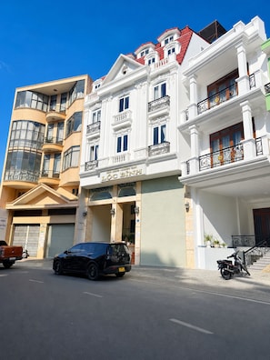 Um edifício com vários andares e entrada no nível da rua, com um carro preto estacionado na frente e uma motocicleta do lado direito.