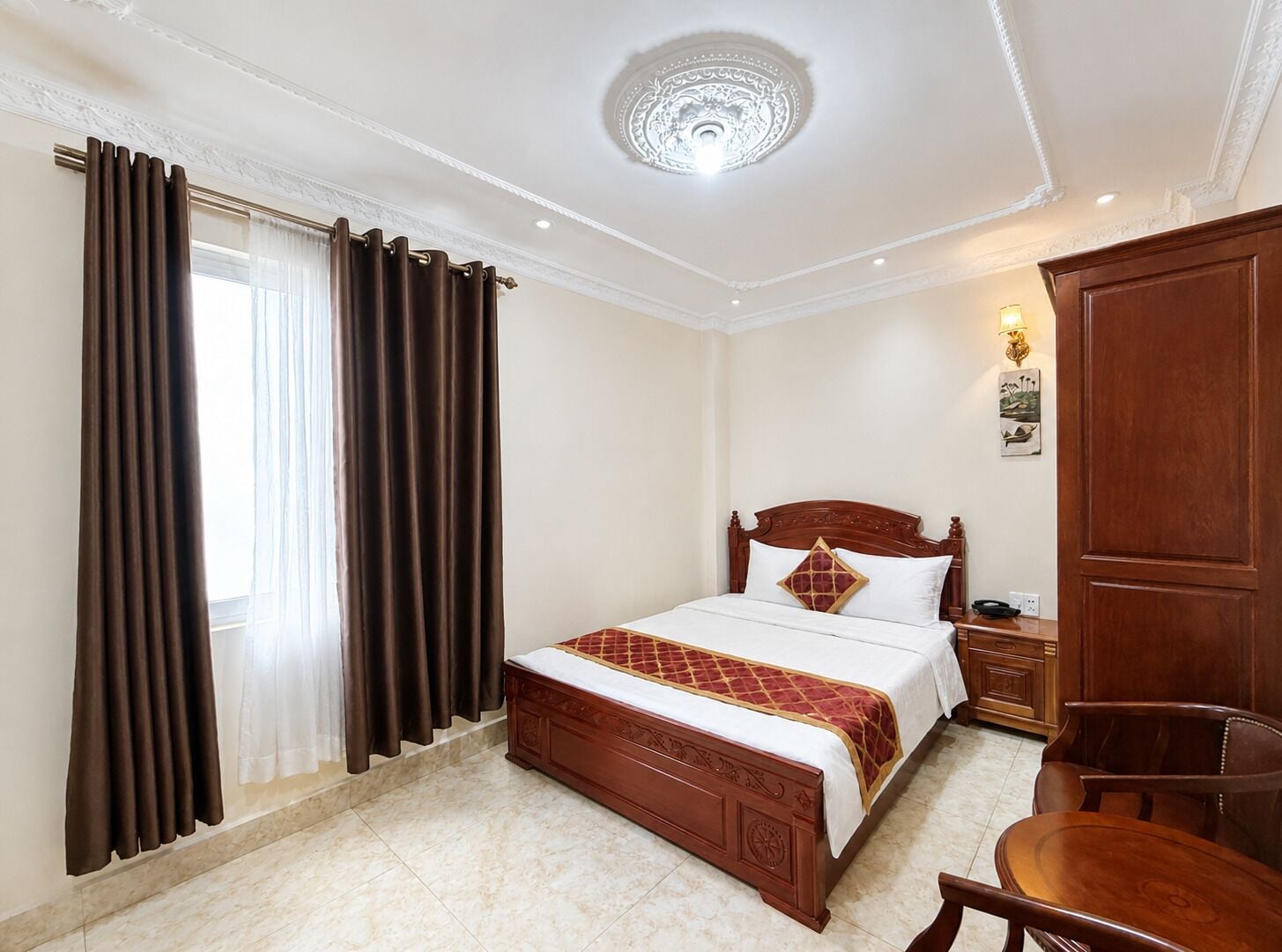 Quarto de hotel com uma cama grande, um guarda-roupa de madeira, uma escrivaninha com cadeira e uma janela com cortinas.