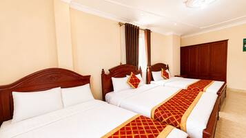 Quarto de hotel com três camas de casal, um guarda-roupa e uma janela grande com cortinas.