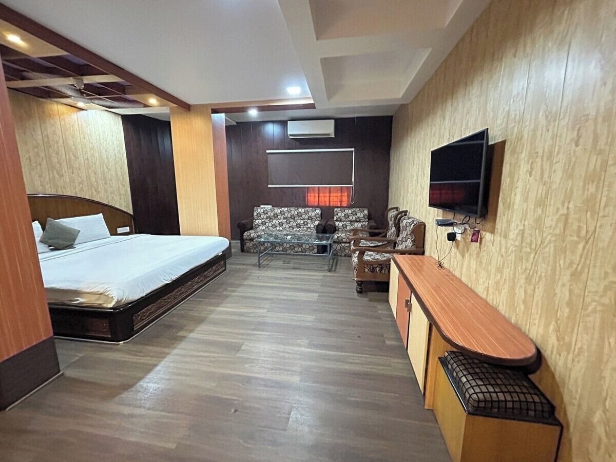 Quarto de hotel com cama, sofá, televisão e secretária.