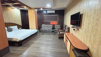 Quarto de hotel com cama, sofá, televisão e secretária.