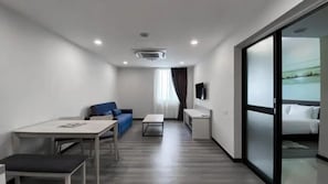 Quarto de hotel com cama, escrivaninha, poltrona, sofá, televisão e porta de correr para uma varanda.