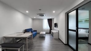 Quarto de hotel com cama, secretária, cadeira, sofá e televisão.