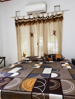Quarto de hotel com uma cama, mesa de cabeceira, ar condicionado e cortinas com estampas de borboletas.