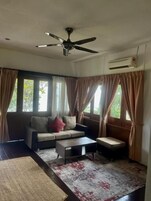 Quarto com ventilador de teto, aparelho de ar condicionado, sofá com almofadas, mesa de centro e tapete estampado.