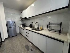 Uma cozinha moderna com armários brancos, eletrodomésticos de aço inoxidável e bancada preta.