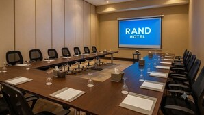 Uma sala de conferências com uma mesa comprida, cadeiras e uma tela de projetor exibindo 'RAND HOTEL'.