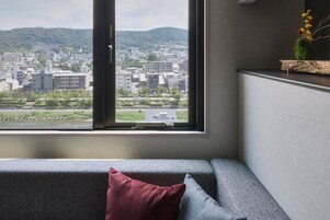 Interior moderno com sofá, janela com vista para a paisagem urbana e uma pequena planta em uma prateleira.