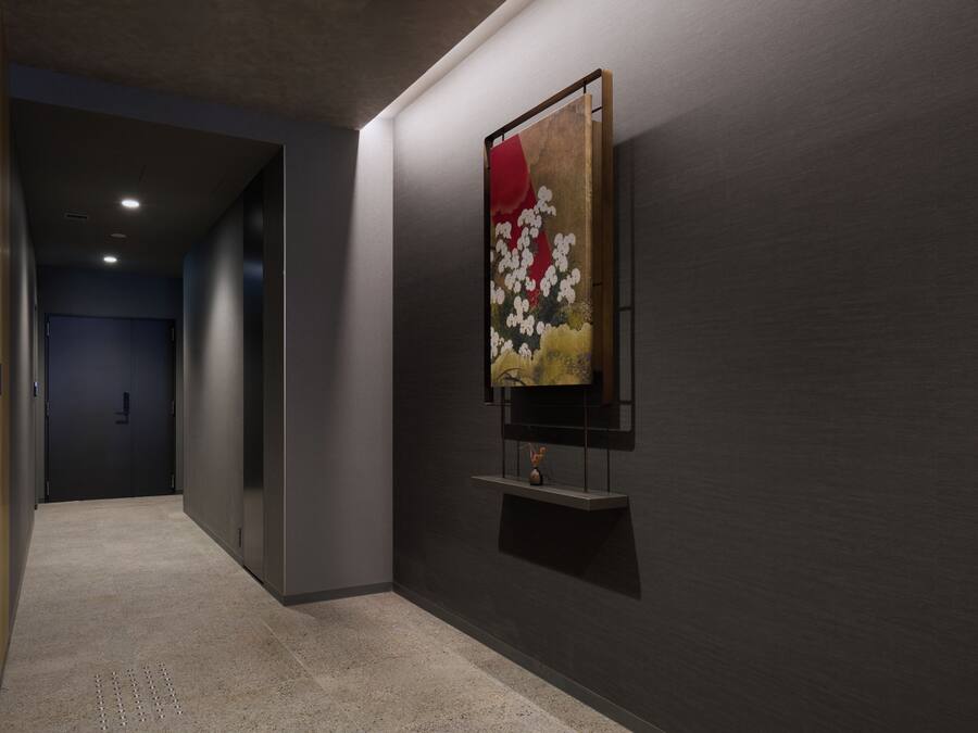 Um corredor com uma obra de arte moderna na parede, uma porta no fim e piso texturizado.