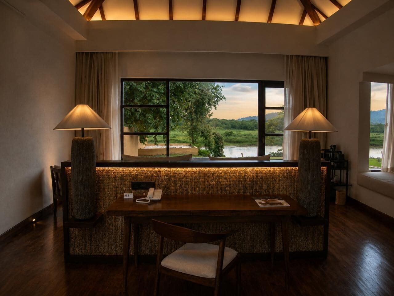 Uma área de refeições com vista para um rio e colinas, com uma mesa comprida, cadeiras e duas luminárias.