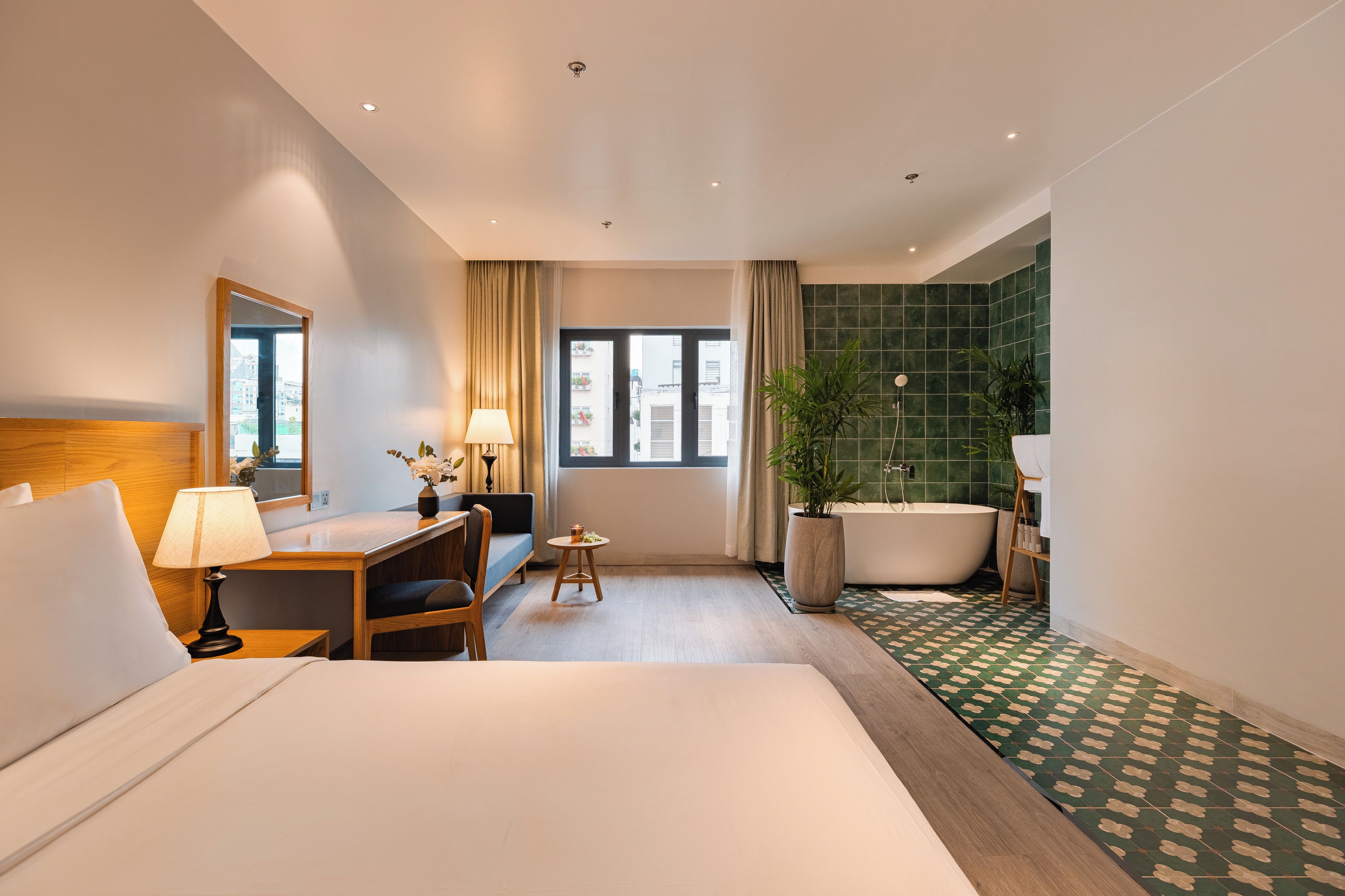 Quarto de hotel com cama, escrivaninha, cadeira, janela, banheiro com banheira e um vaso de planta.