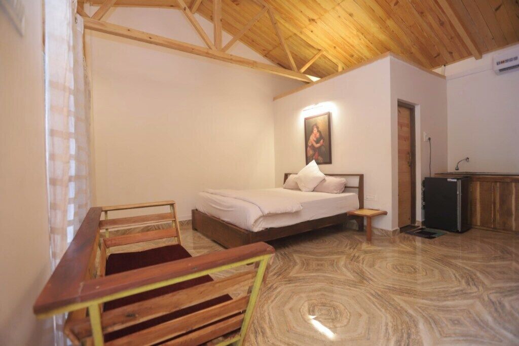 Quarto com cama, um banco de madeira, uma mesinha e um frigorífico.
