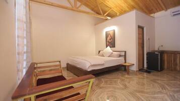 Quarto com cama, um banco de madeira, uma mesinha e um frigorífico.