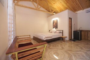 Quarto com cama, um banco de madeira, uma mesinha e um frigorífico.