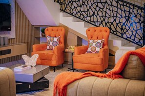 Uma sala de estar moderna com dois poltronas laranjas, uma mesa de centro e uma estante.