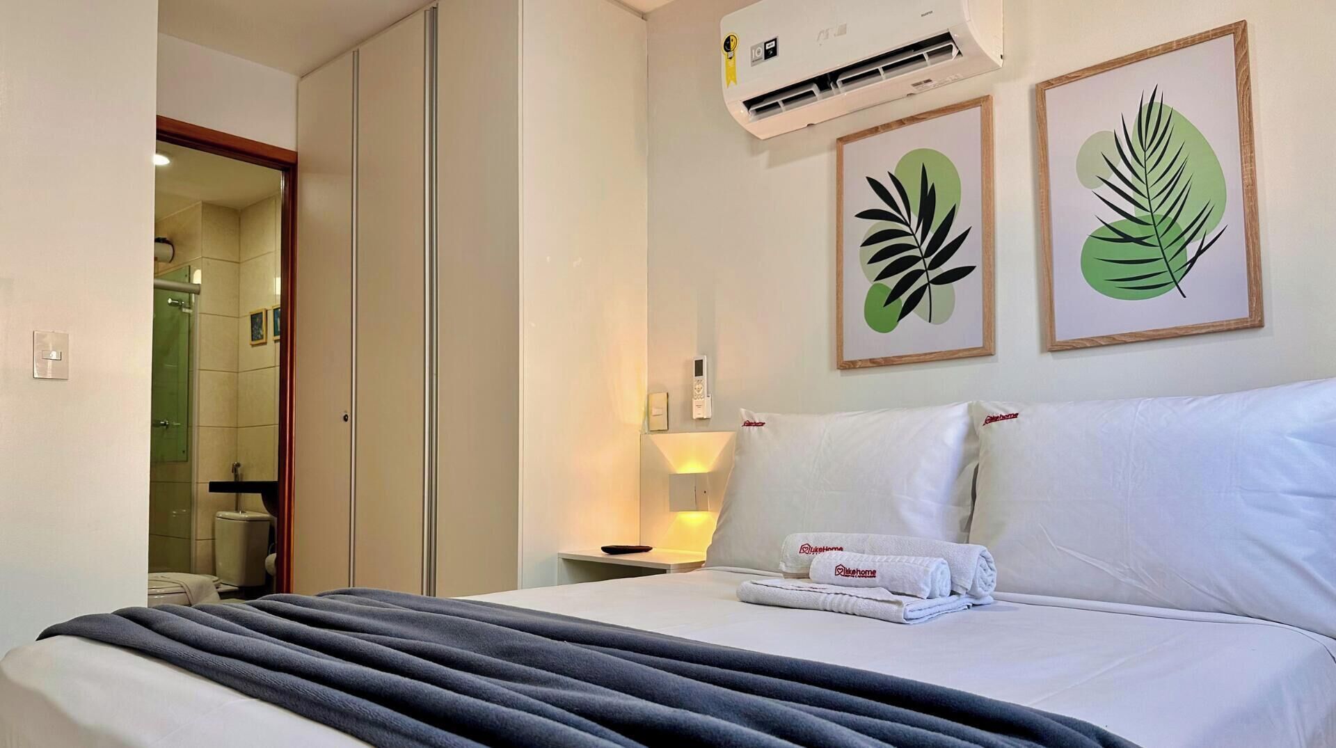 Quarto de hotel com uma cama, abajur, toalha e duas obras de arte com folhas emolduradas na parede.