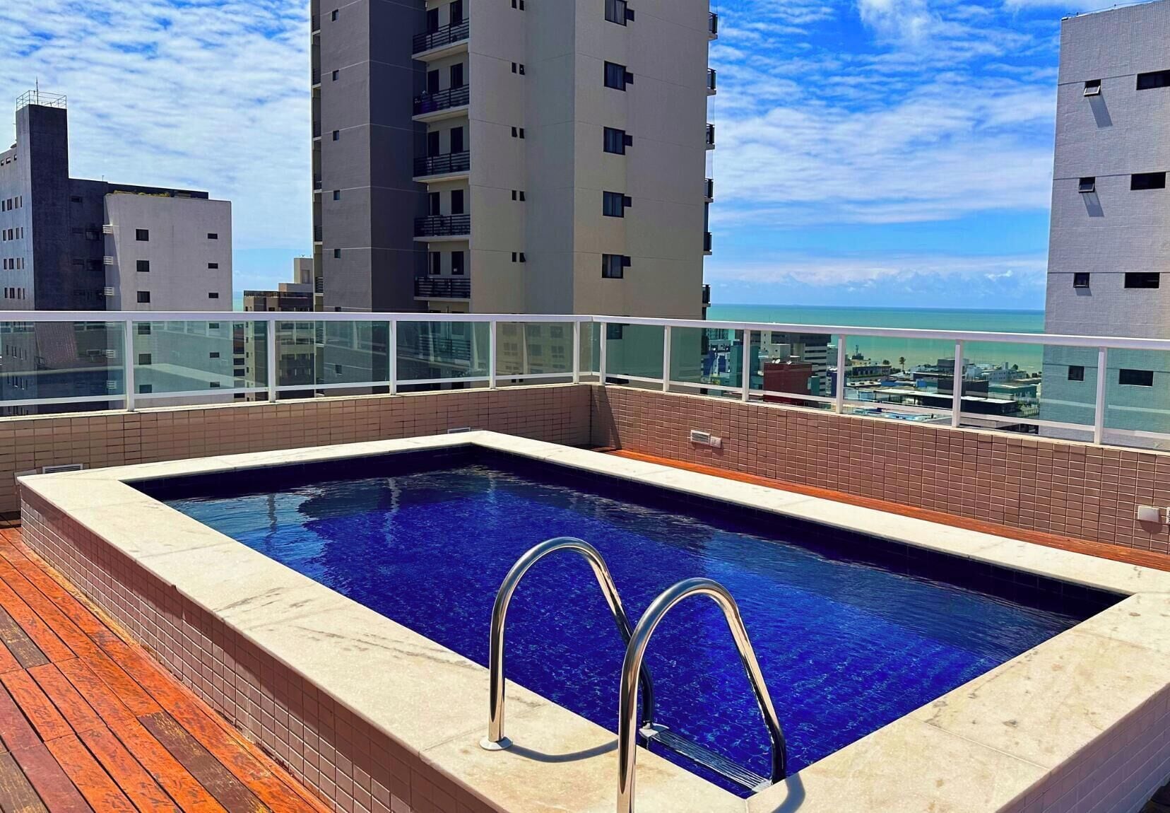 Piscina no terraço com vista para o oceano e edifícios ao redor.