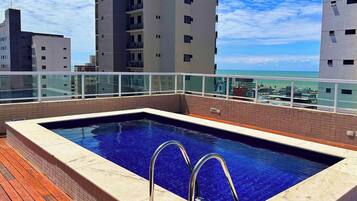 Piscina no terraço com vista para o oceano e edifícios ao redor.