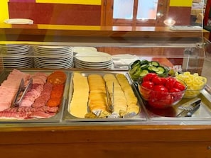Buffet com diversas opções de comida, incluindo carnes fatiadas, queijos e legumes.