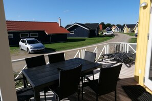 Um terraço com mobiliário externo, vista para uma rua com casas e um carro estacionado.