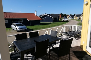 Um terraço com mobiliário externo, vista para uma rua com casas e um carro estacionado.