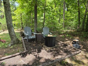 Um camping com duas cadeiras Adirondack, um braseiro portátil e uma churrasqueira.