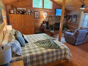 Interior acolhedor de uma cabana, com uma cama, lareira e televisão fixada na parede.